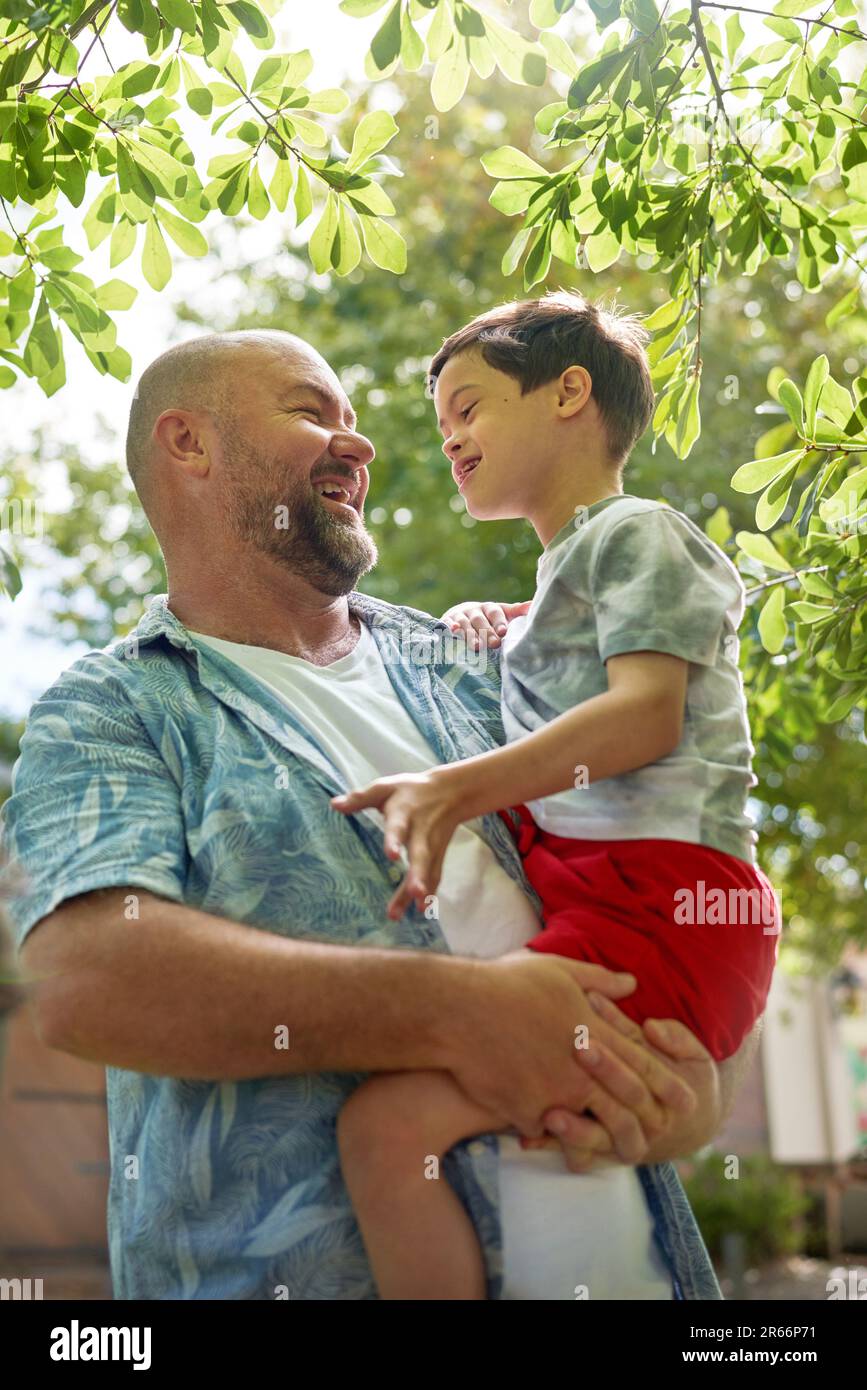 Happy father holding cute son with Down Syndrome below tree Stock Photo ...