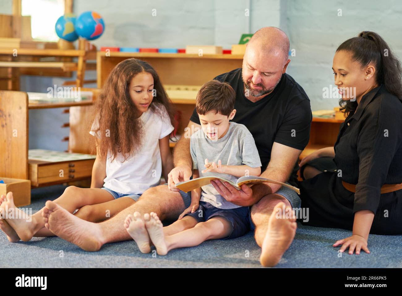 Barefoot family reading book on floor at home Stock Photo - Alamy