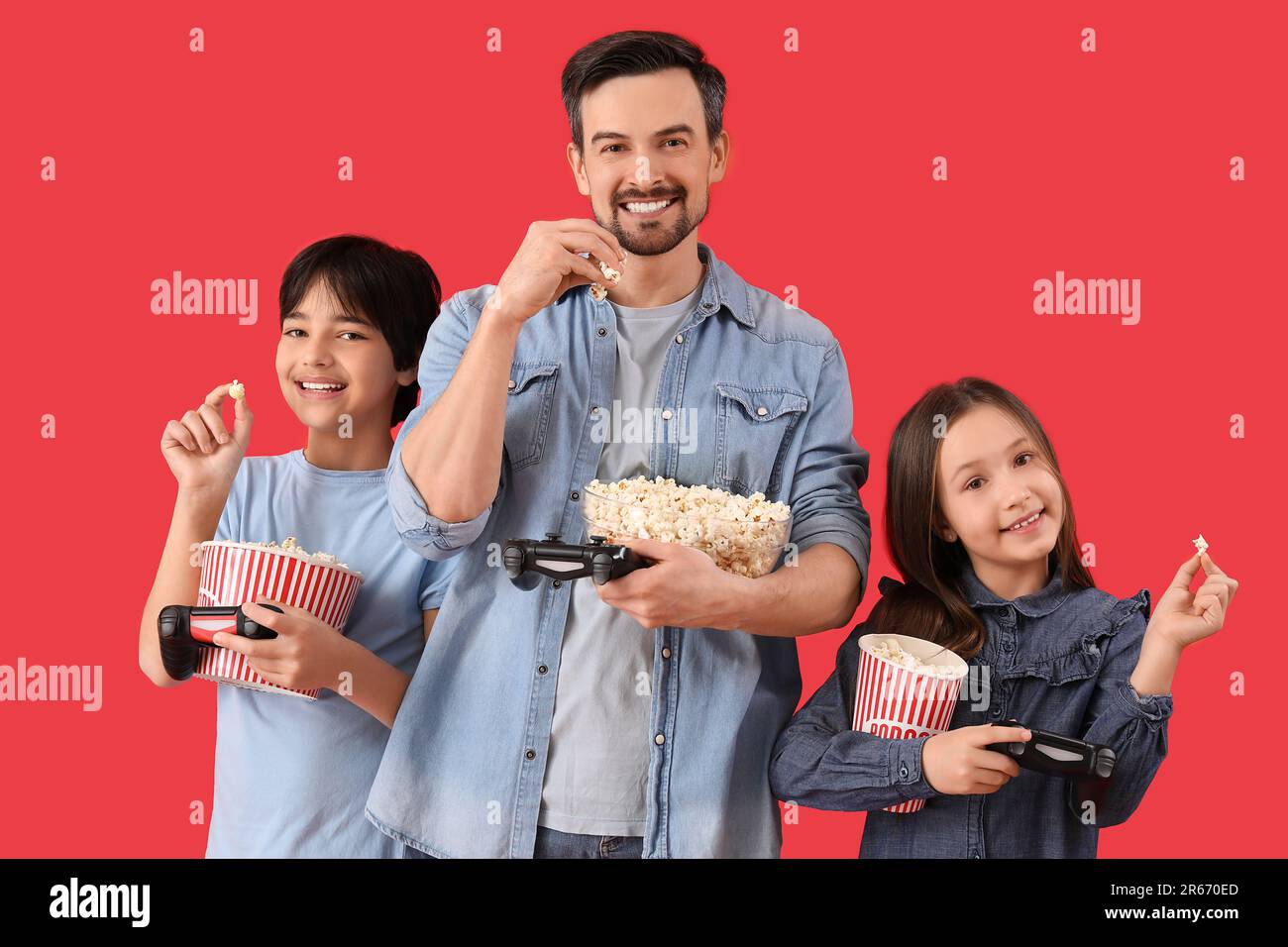 Little children with their father and game pads eating popcorn on red ...