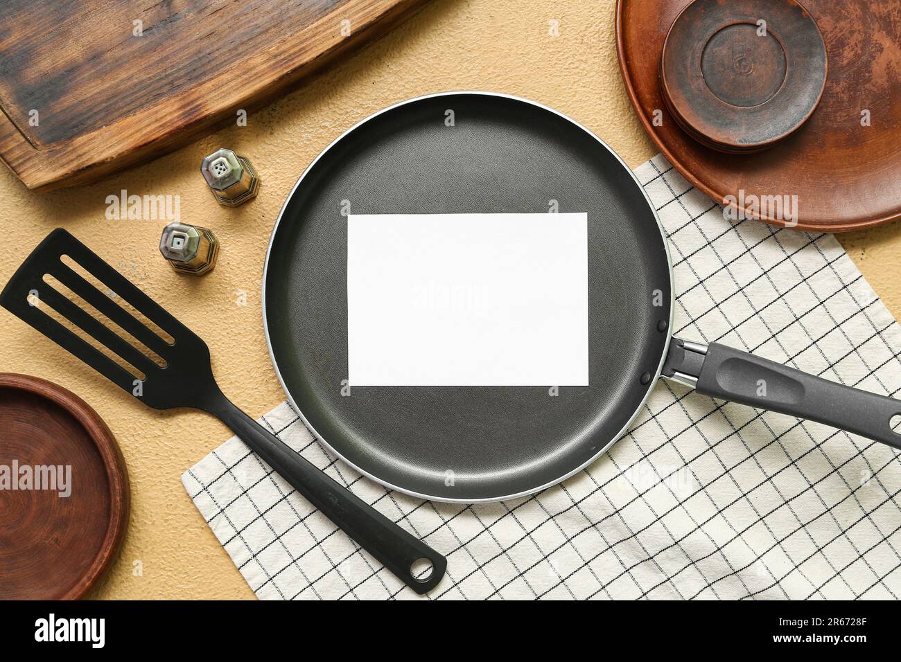 Frying pan with blank card and kitchen utensils on beige background ...