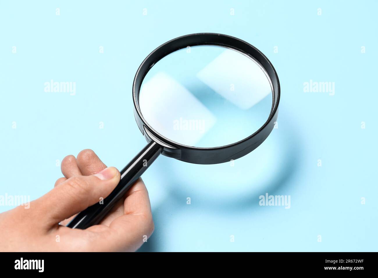 Female hand with magnifier on blue background Stock Photo - Alamy