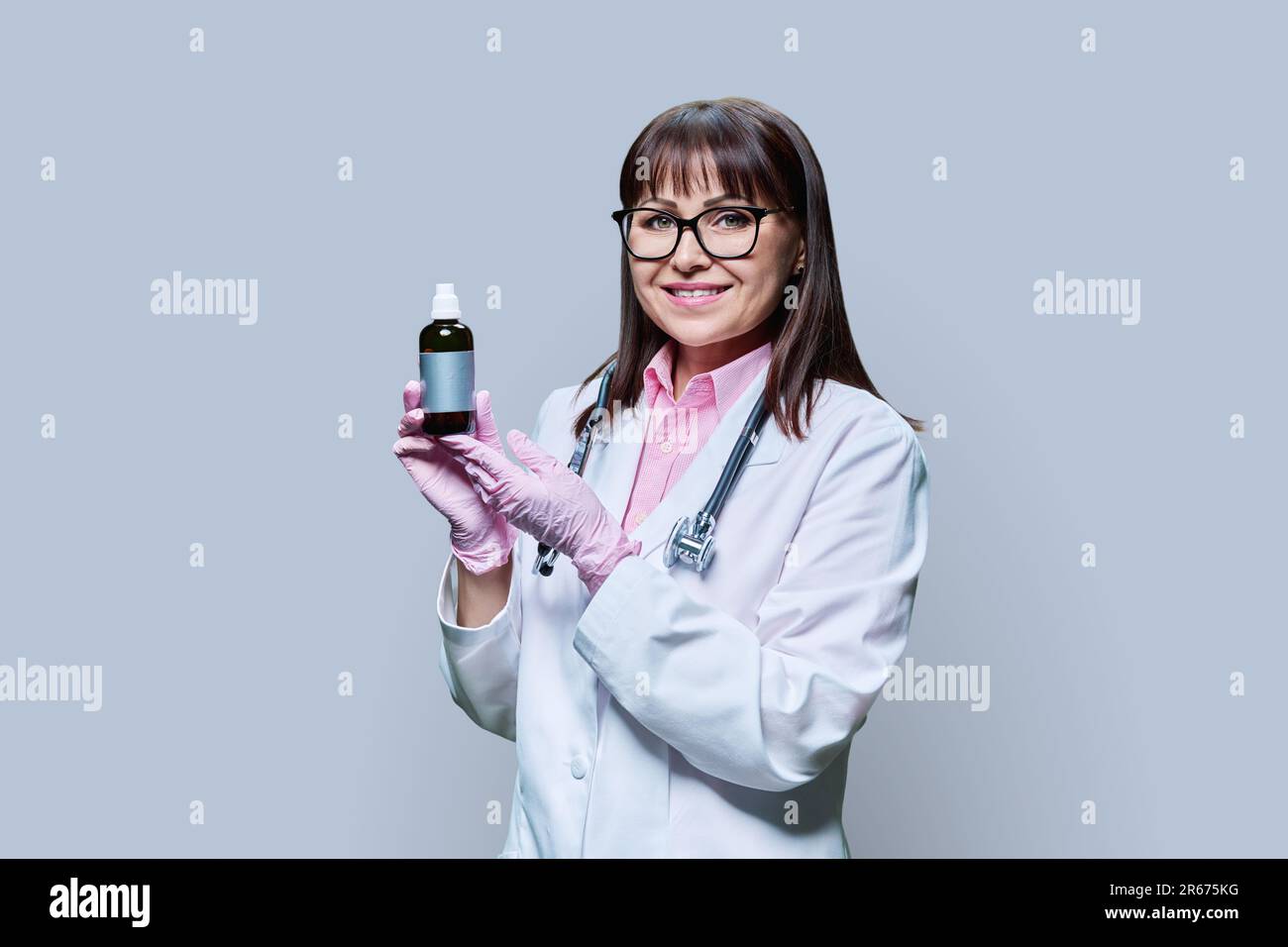 Woman doctor showing glass liquid medicine bottle, grey studio ...
