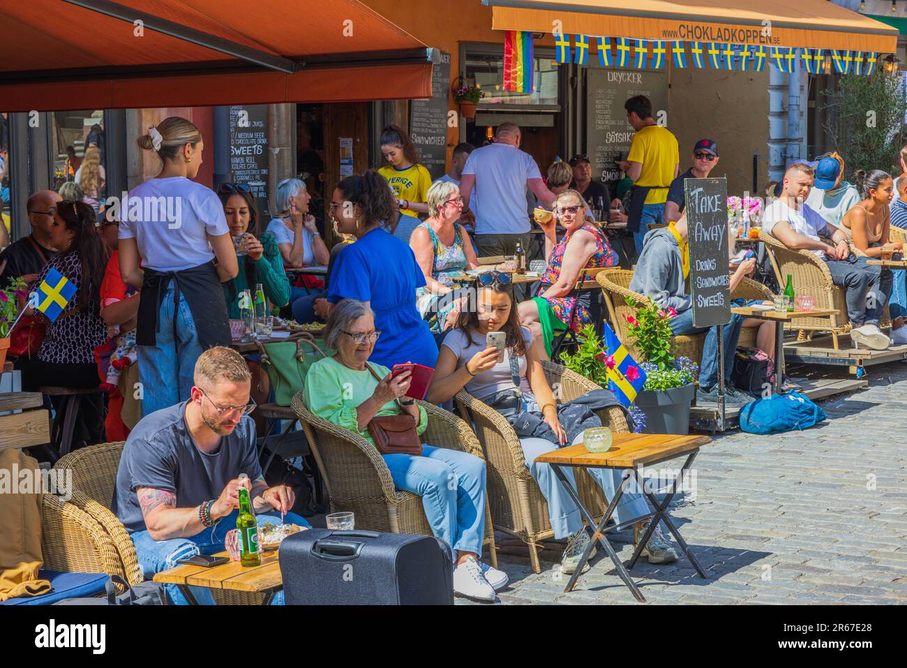 View of people in outdoor café decorated with Swedish flags in honor of ...