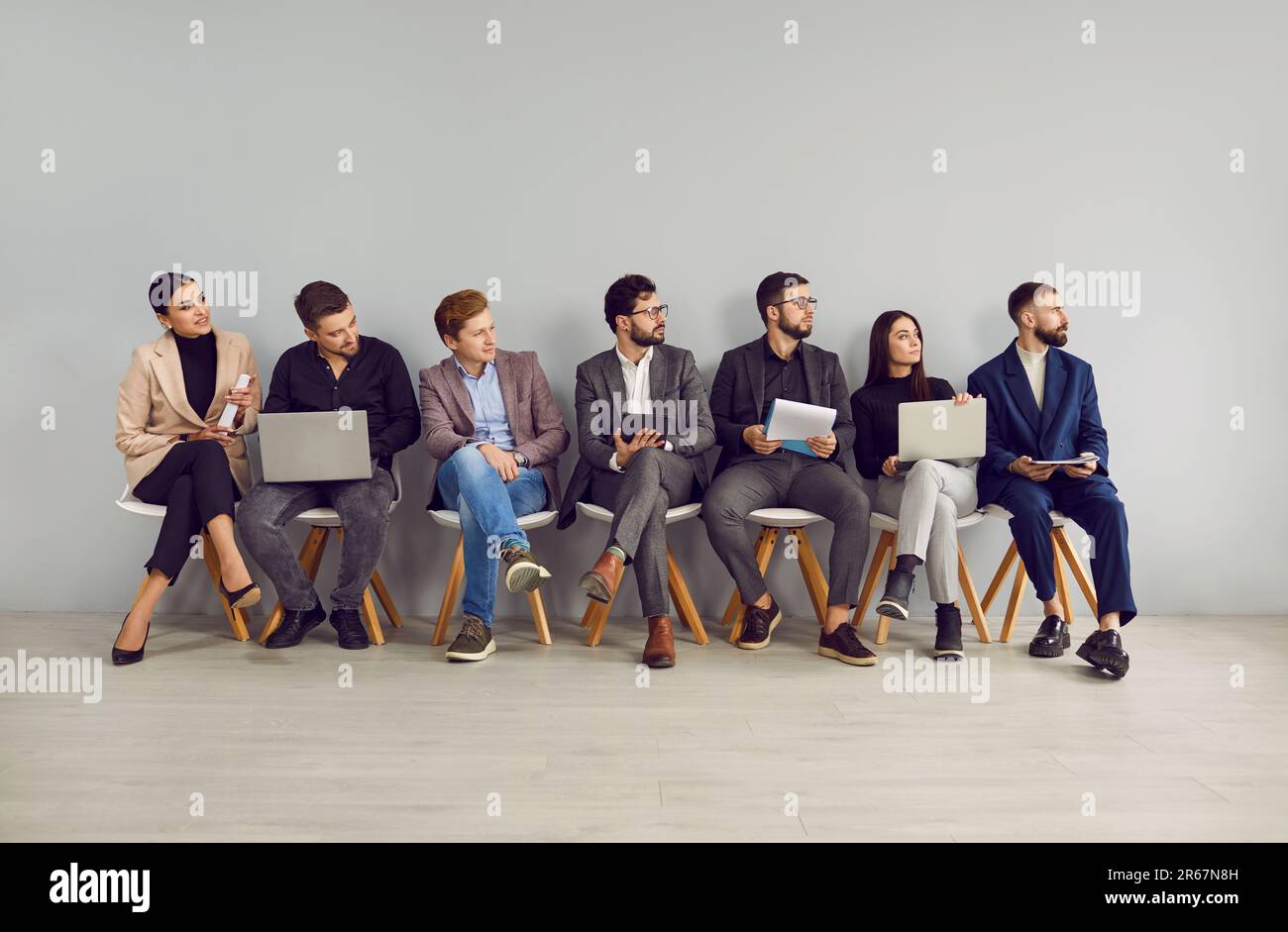 Group of men and women sitting by a gray office wall and waiting for a ...