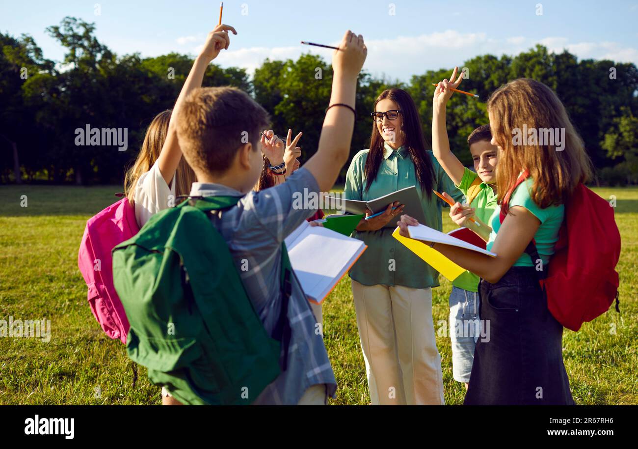 Group of children who are having class in nature raise hands to answer ...