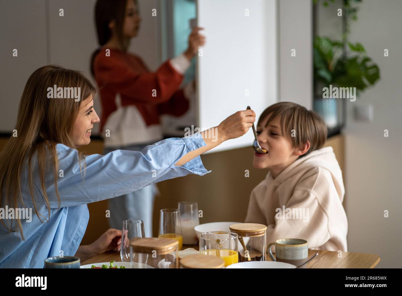 Happy young mother with child have fun breakfast. Mom feeds teenage son ...