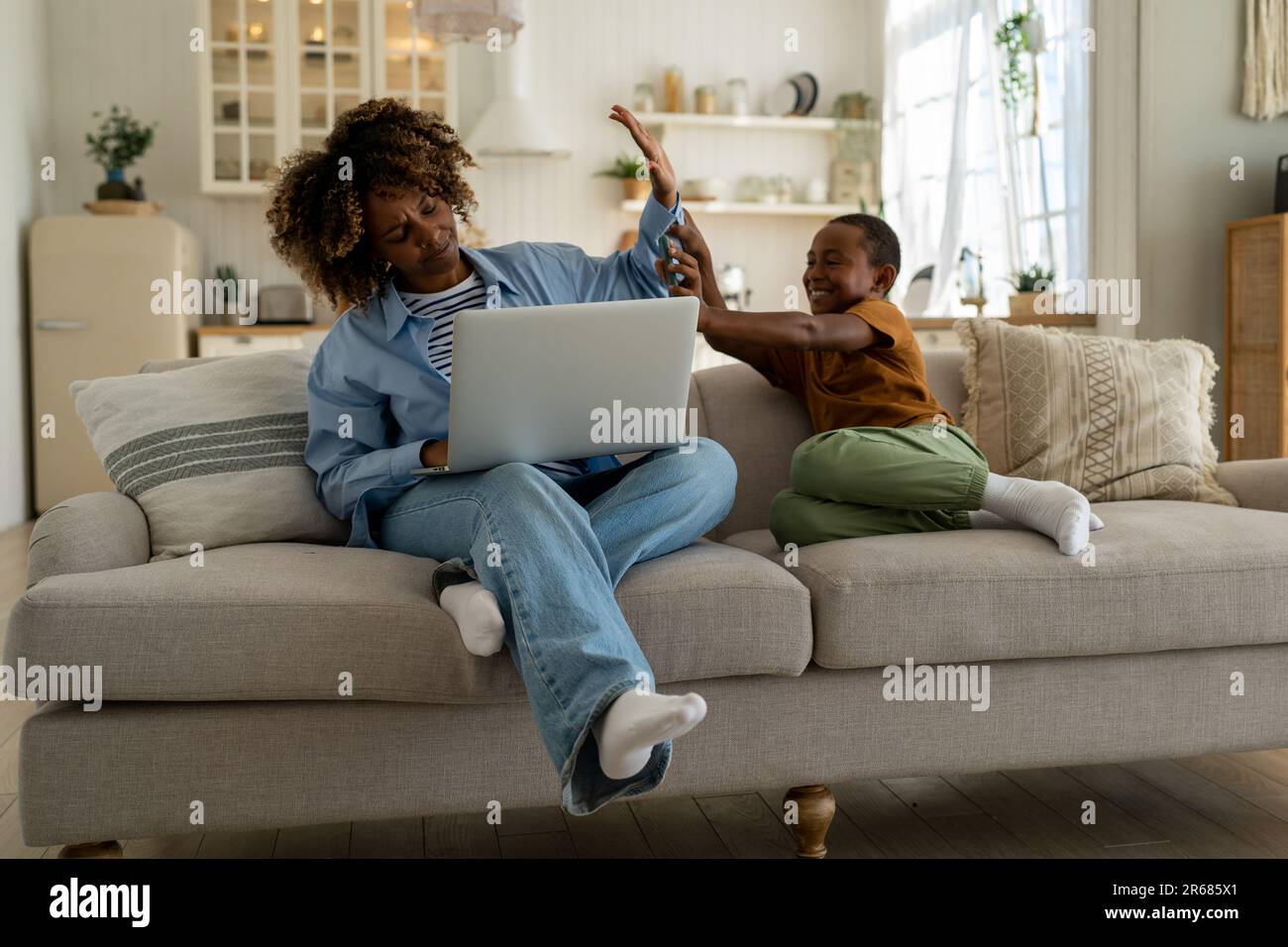 Small child disturbing work-at-home mom.Displeased young african ...