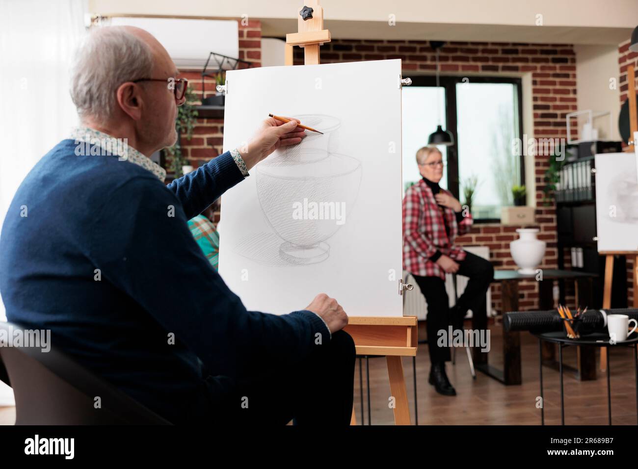 Senior man student sitting at easel using pencil drawing on canvas ...