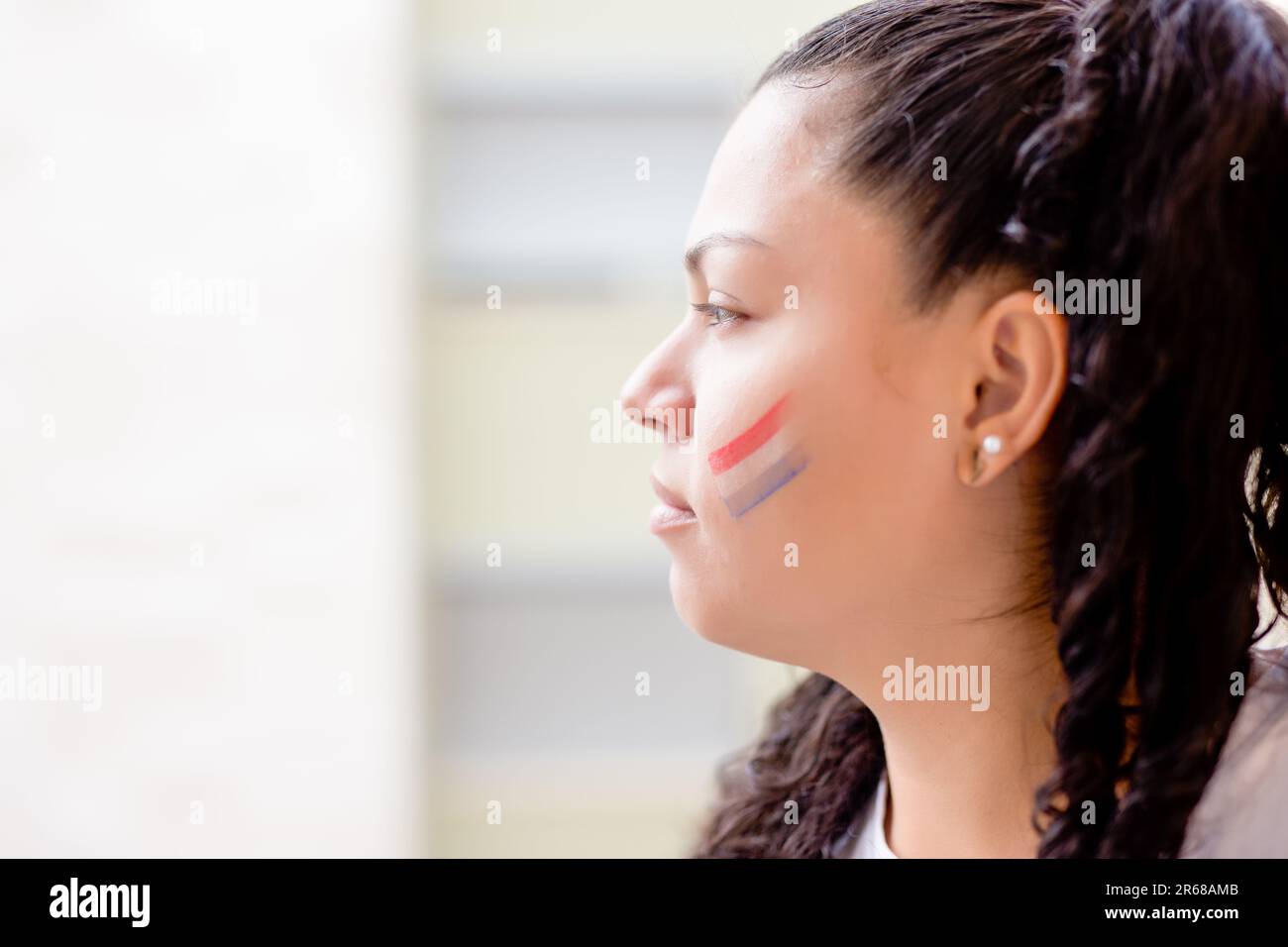 A young woman with a Dutch flag painted on her cheek, celebrating in a ...