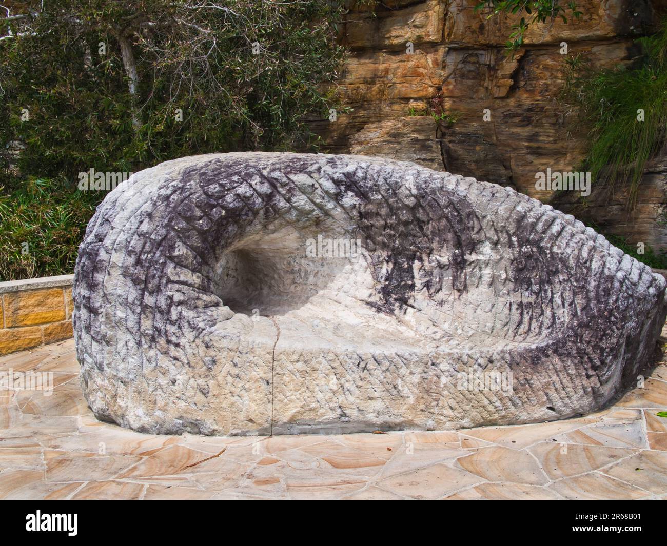 A modern grey concrete bench sits adjacent to a cliff face along a ...