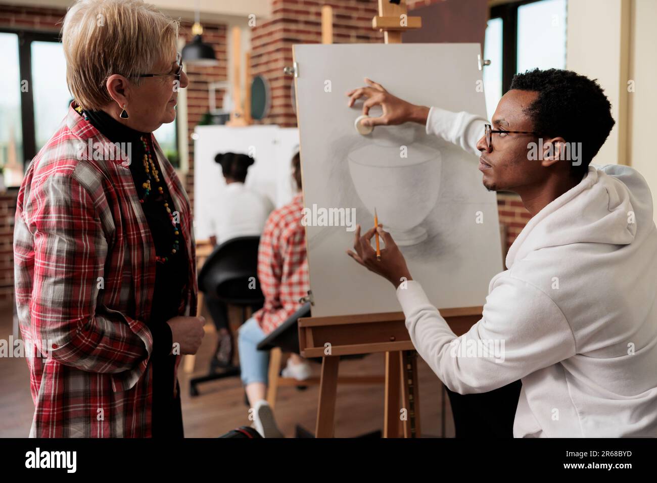 Senior woman taking up drawing class in art studio, listening to ...