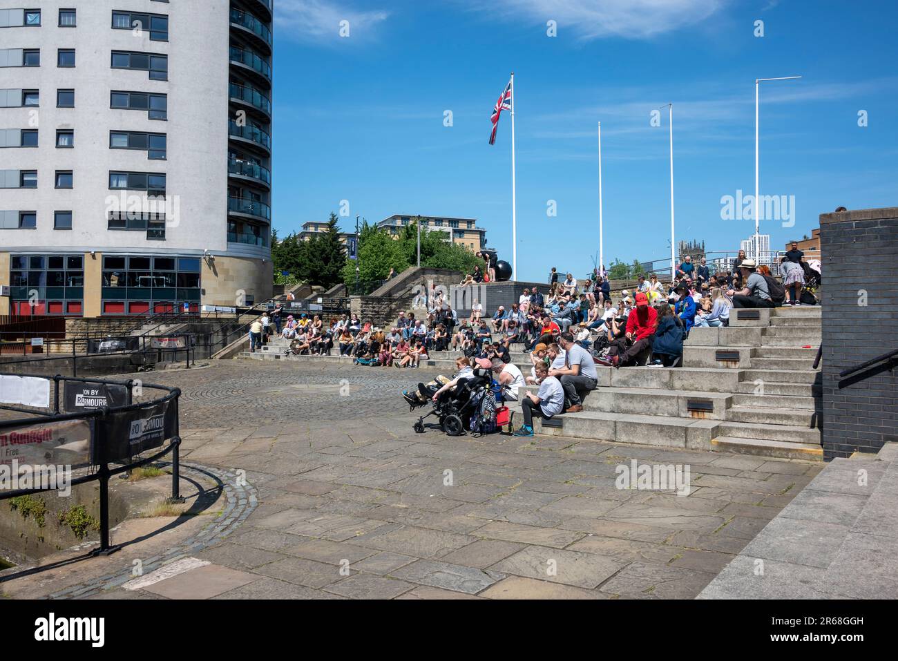 People sitting on the steps of the open air amphitheatre area of Leeds ...