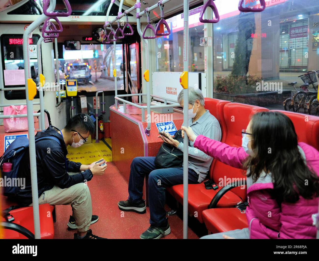 Interior of a public transportation bus in Taipei, Taiwan with three seated passengers; three ...