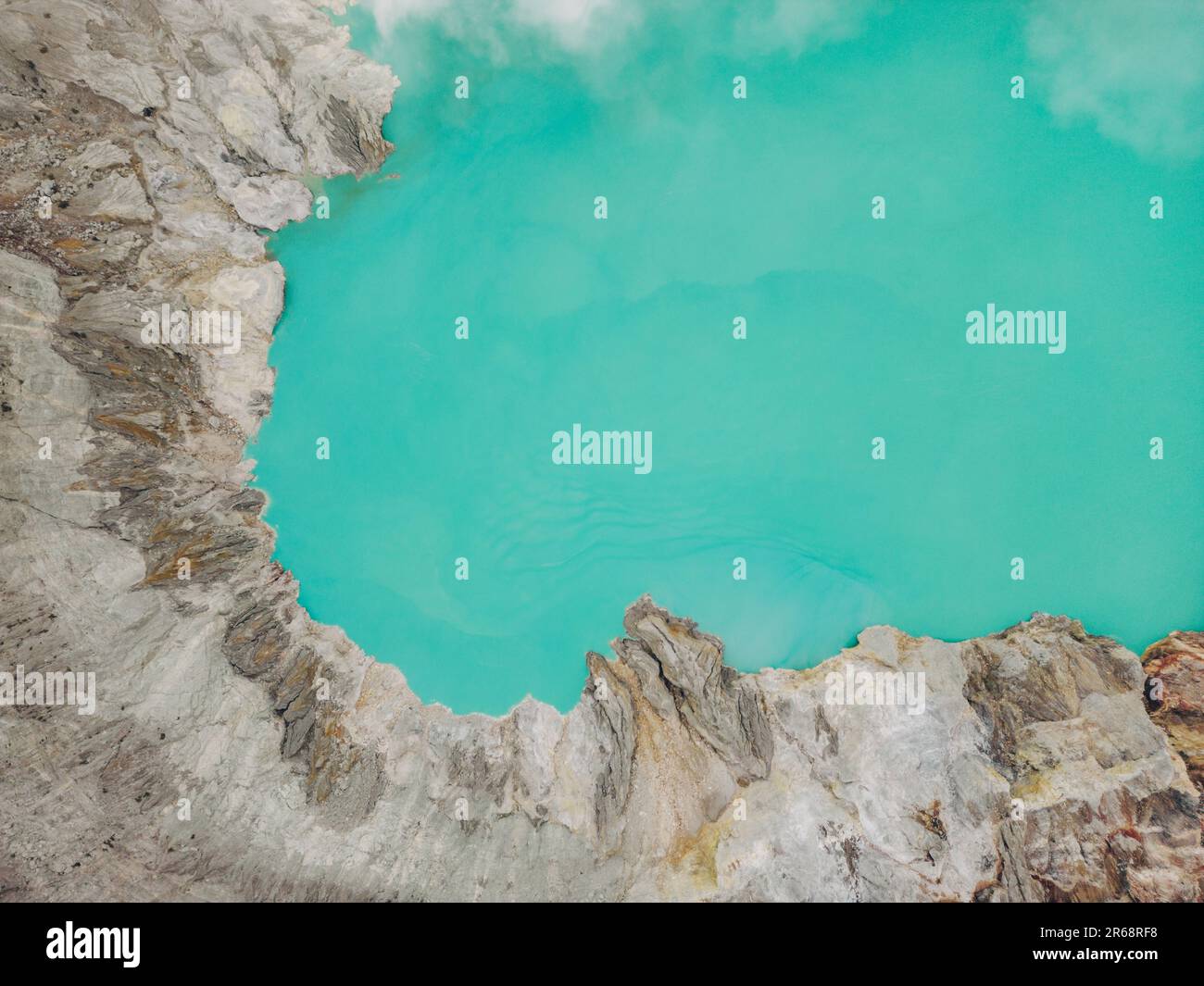 Top aerial view of turquoise sulfur water lake, surrounded by rock cliff at Kawah Ijen volcano ...