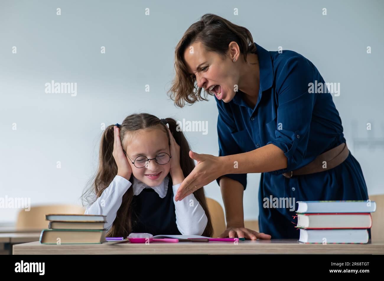 A female teacher yells at a student. Little girl covers her ears with ...