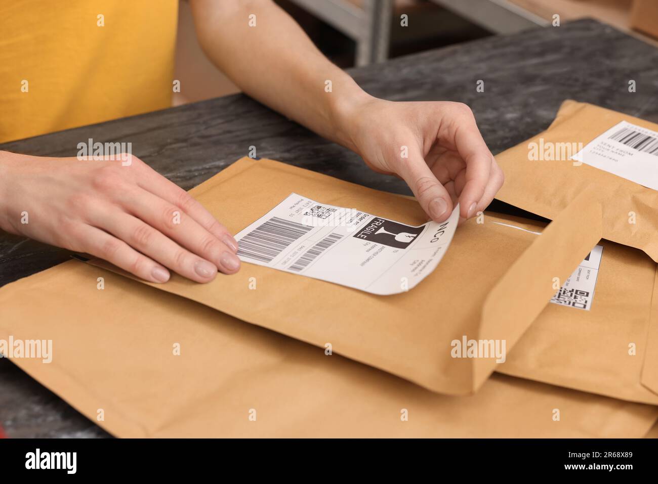 Post office worker sticking barcode on parcel at counter indoors ...