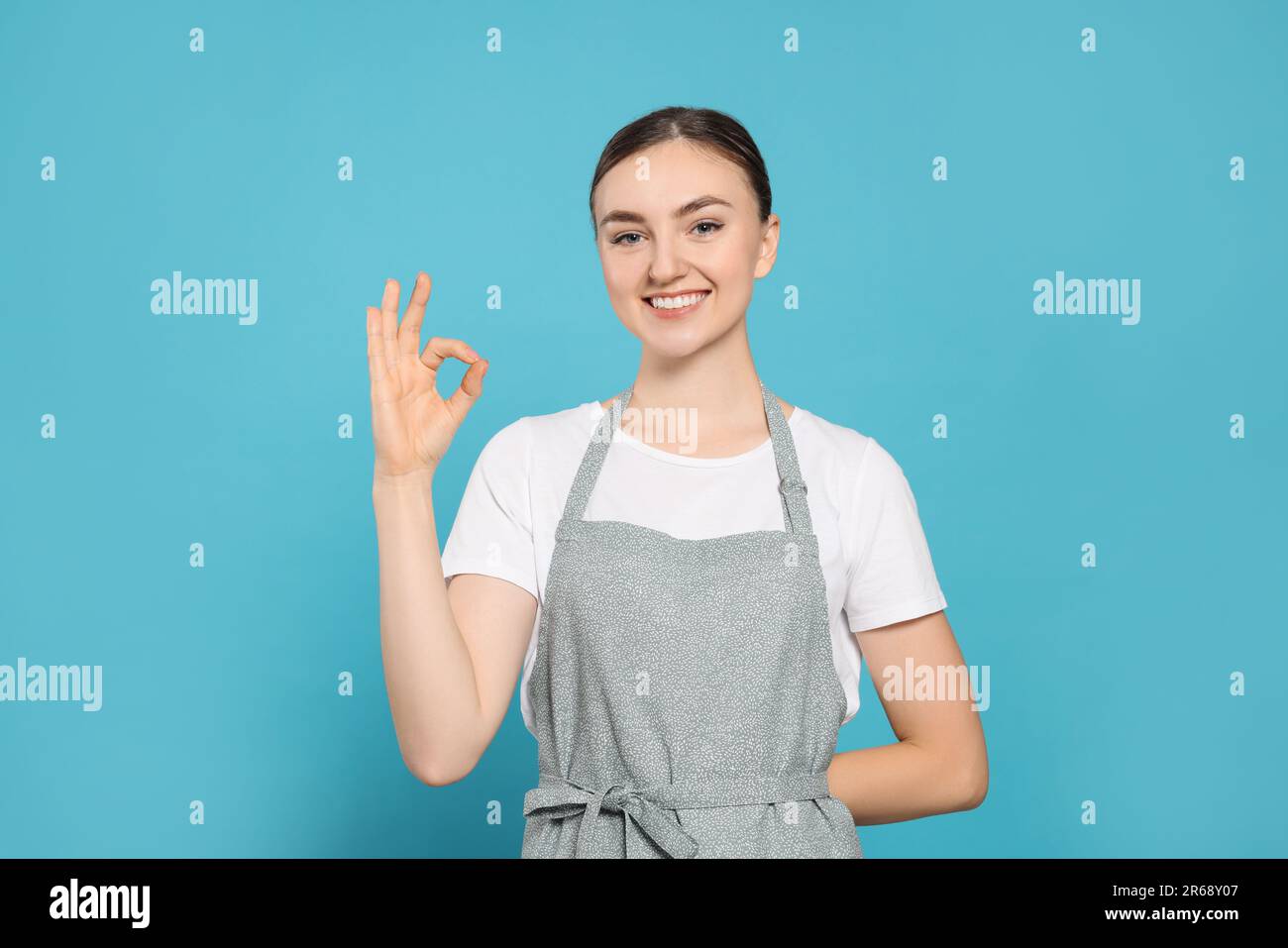 Beautiful young woman in clean apron with pattern on light blue ...