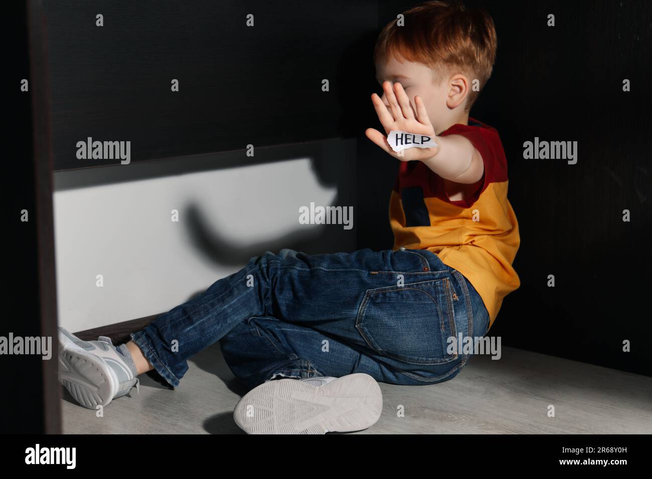 Scared little boy holding piece of paper with word Help on floor at ...