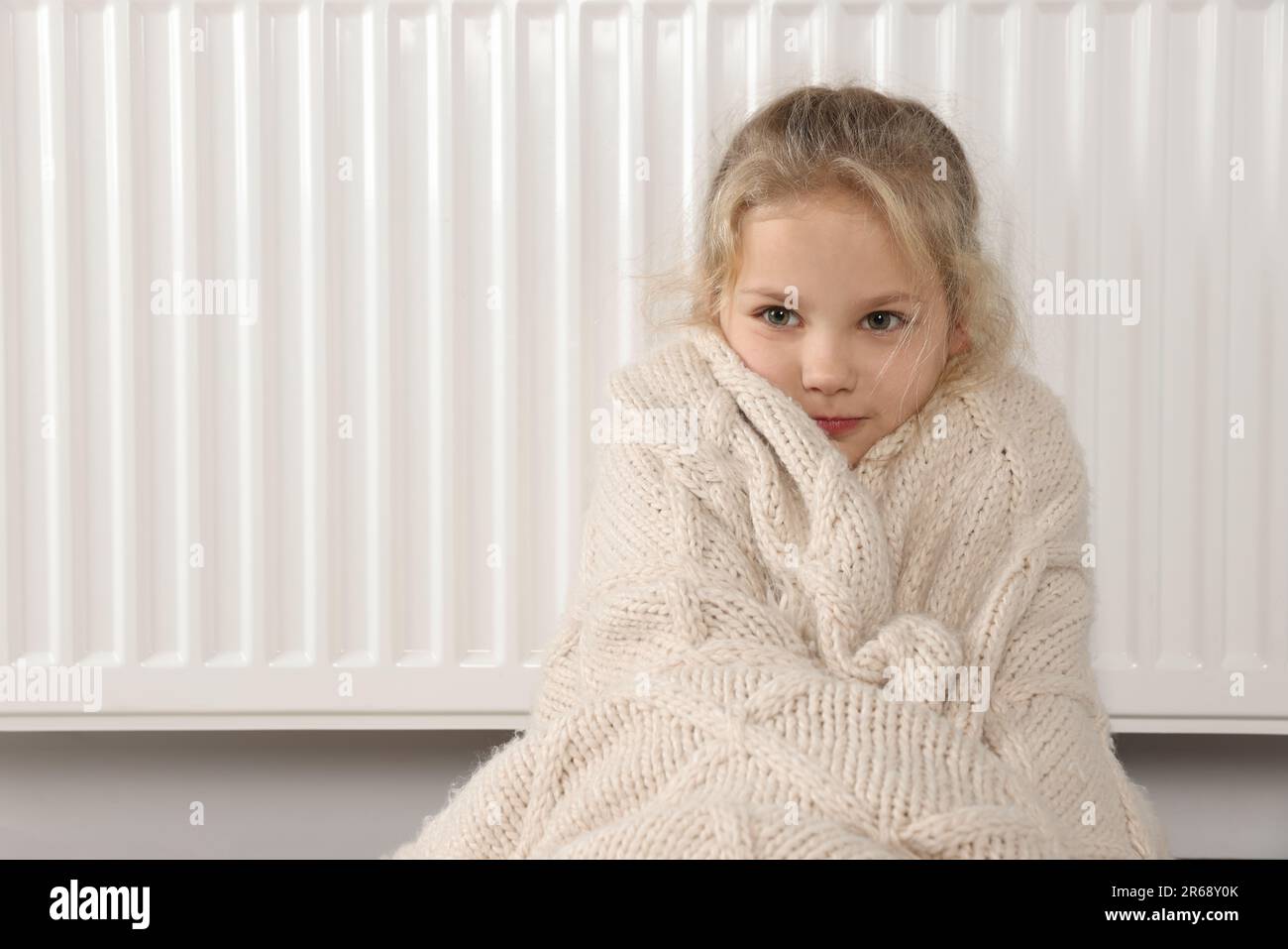 Little girl covered with knitted plaid sitting near heating radiator at ...