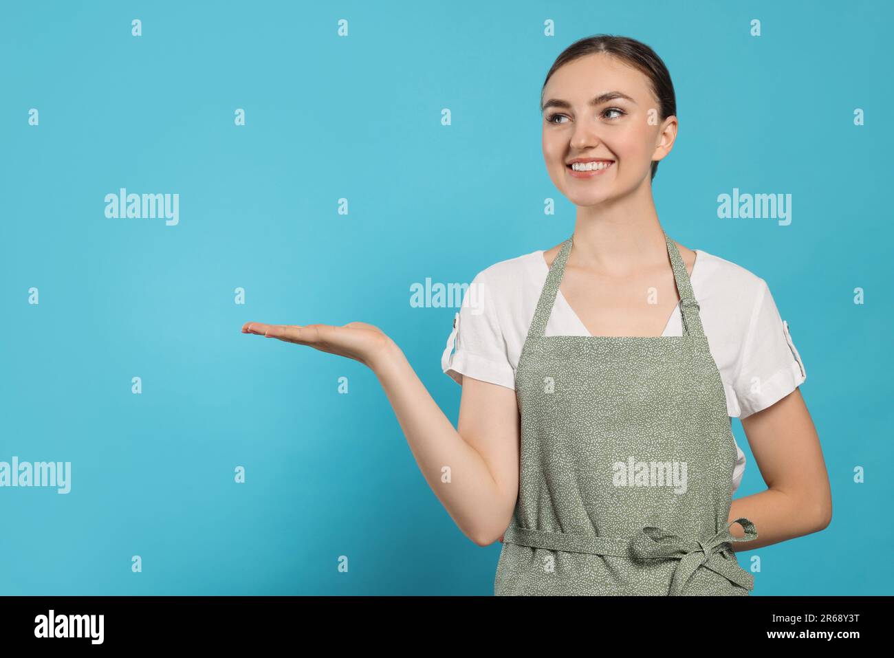 Beautiful young woman in clean apron with pattern on light blue ...