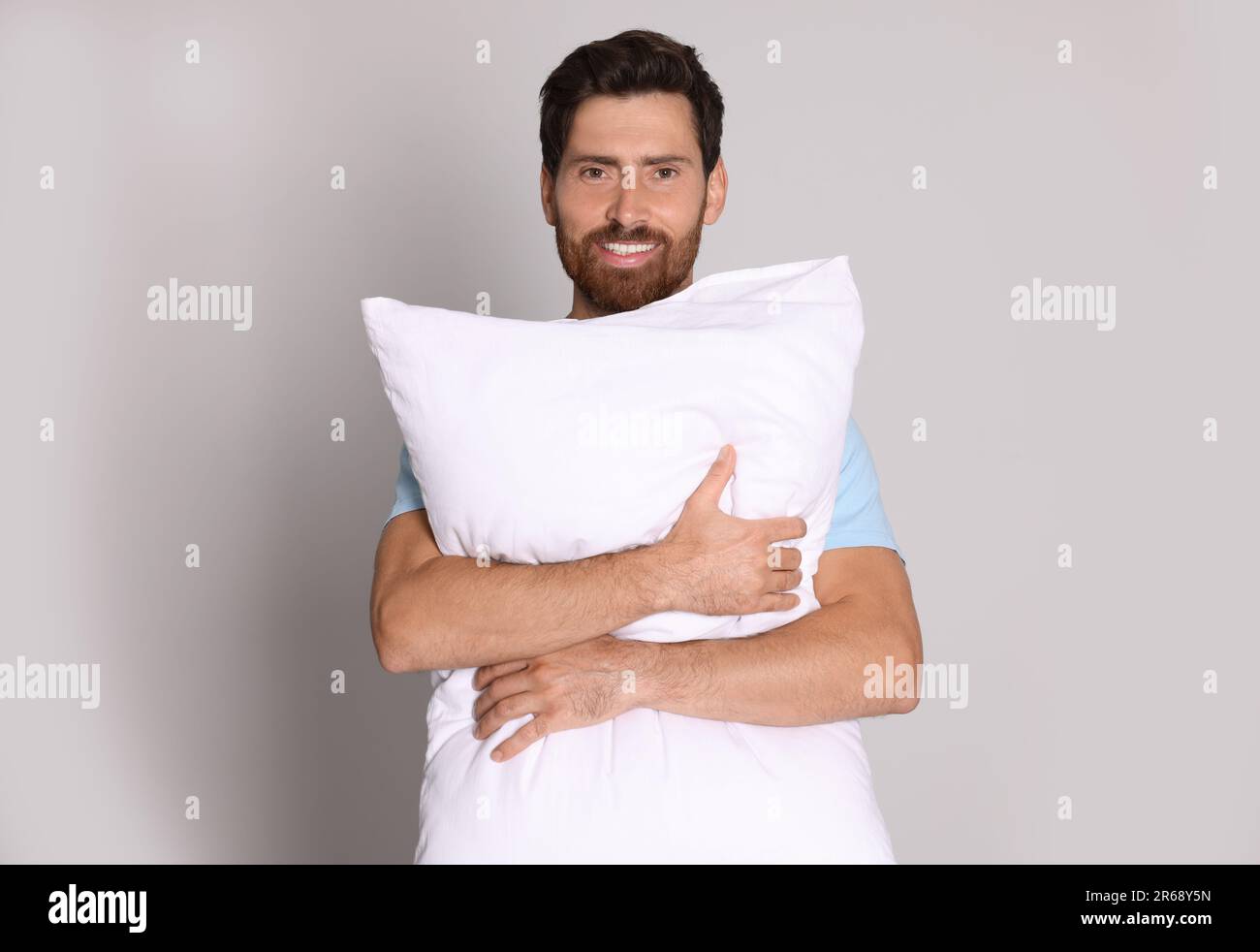 Smiling handsome man hugging soft pillow on light grey background Stock ...