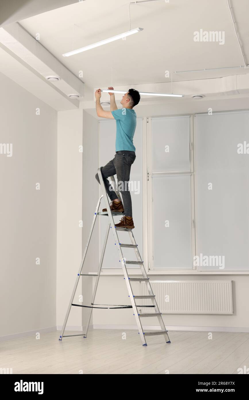 Young man installing ceiling lamp on stepladder indoors Stock Photo - Alamy