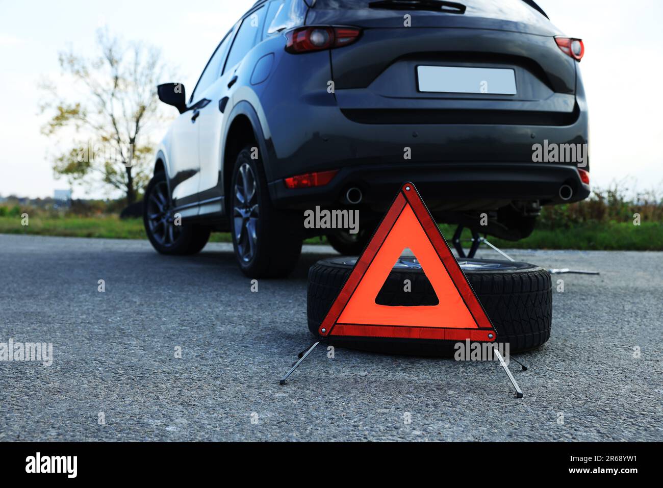 Emergency warning triangle and tire near car on roadside Stock Photo ...