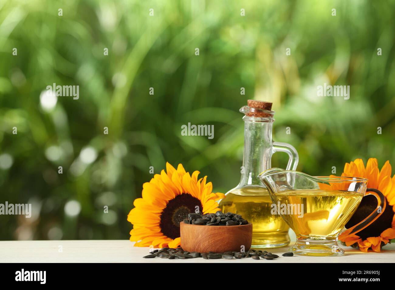 Sunflower cooking oil, seeds and yellow flowers on white wooden table ...