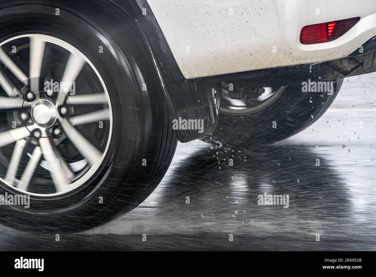 Detail of the rear wheel of a car driving in the rain on a wet road ...