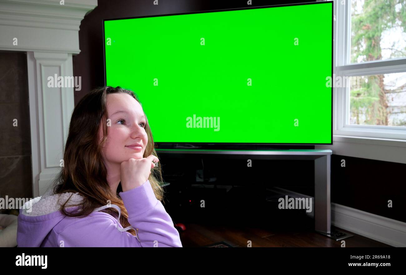 teenage girl sits admiringly in front of a big green chroma key tv ...