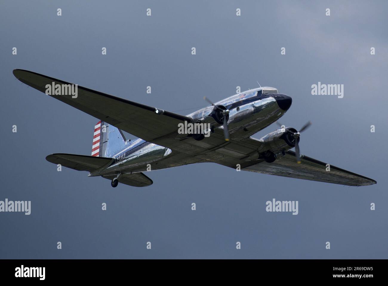 A silver Douglas C-47 Skytrain soaring in the sky against white clouds ...