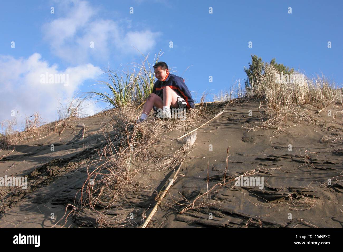 Teenage boy sliding down sand dunes at Lake Wainamu, Bethells beach ...