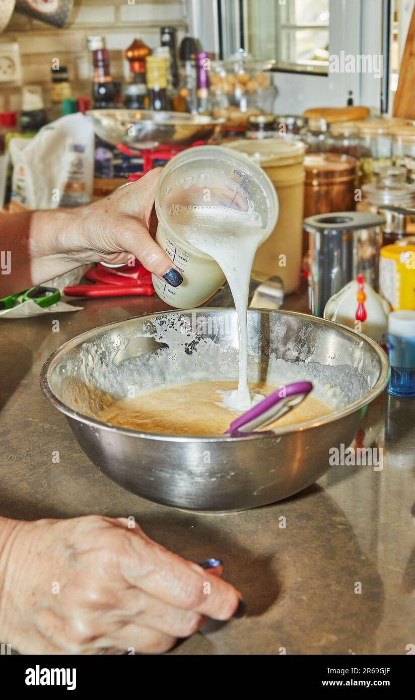 Chef in the home kitchen pours milk from measuring glass into pot with ...