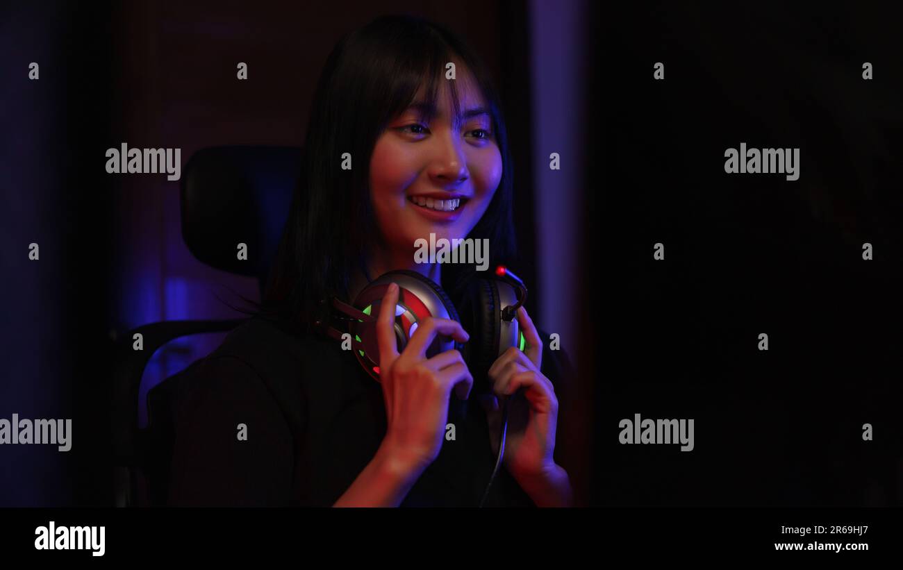 Female cyber hacker gamer in headphone around neck watching video games on monitor with having ...