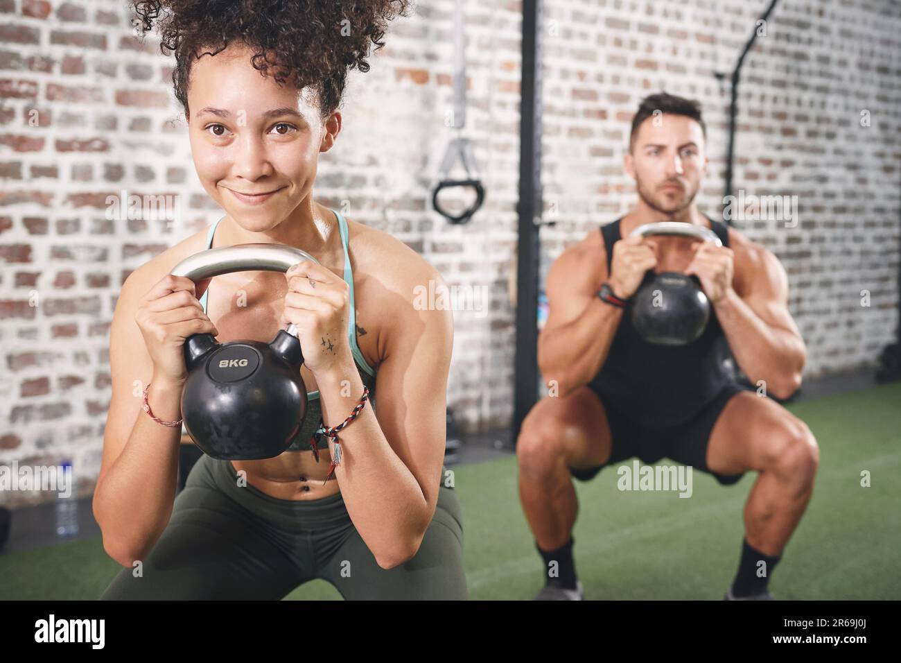Make every squat count. two sporty young people using kettlebells while ...