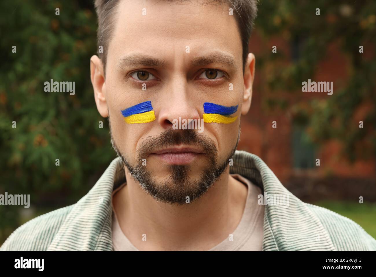 Angry man with drawings of Ukrainian flag on face outdoors, closeup ...