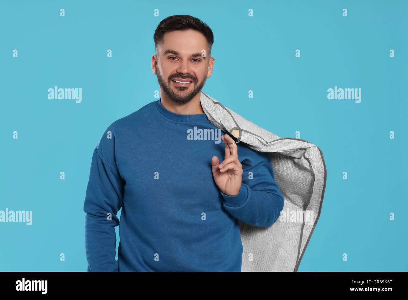 Man holding garment cover with clothes on light blue background. Dry ...
