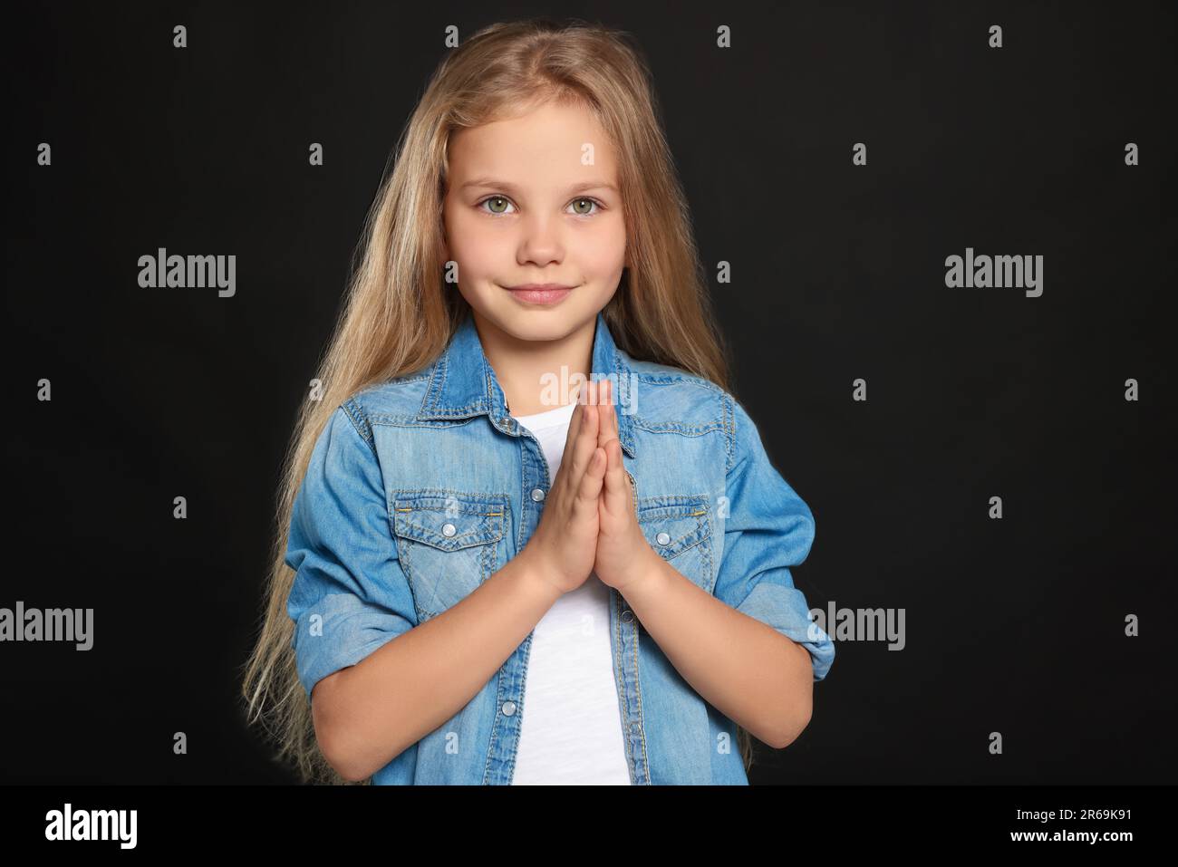 Girl with clasped hands praying on black background Stock Photo - Alamy