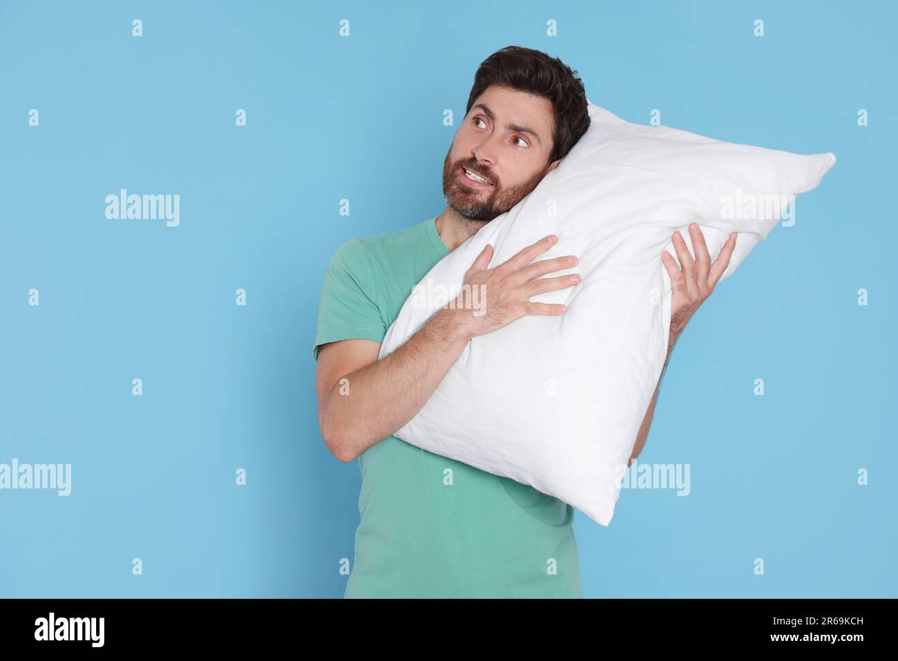 Smiling handsome man hugging soft pillow on light blue background Stock ...