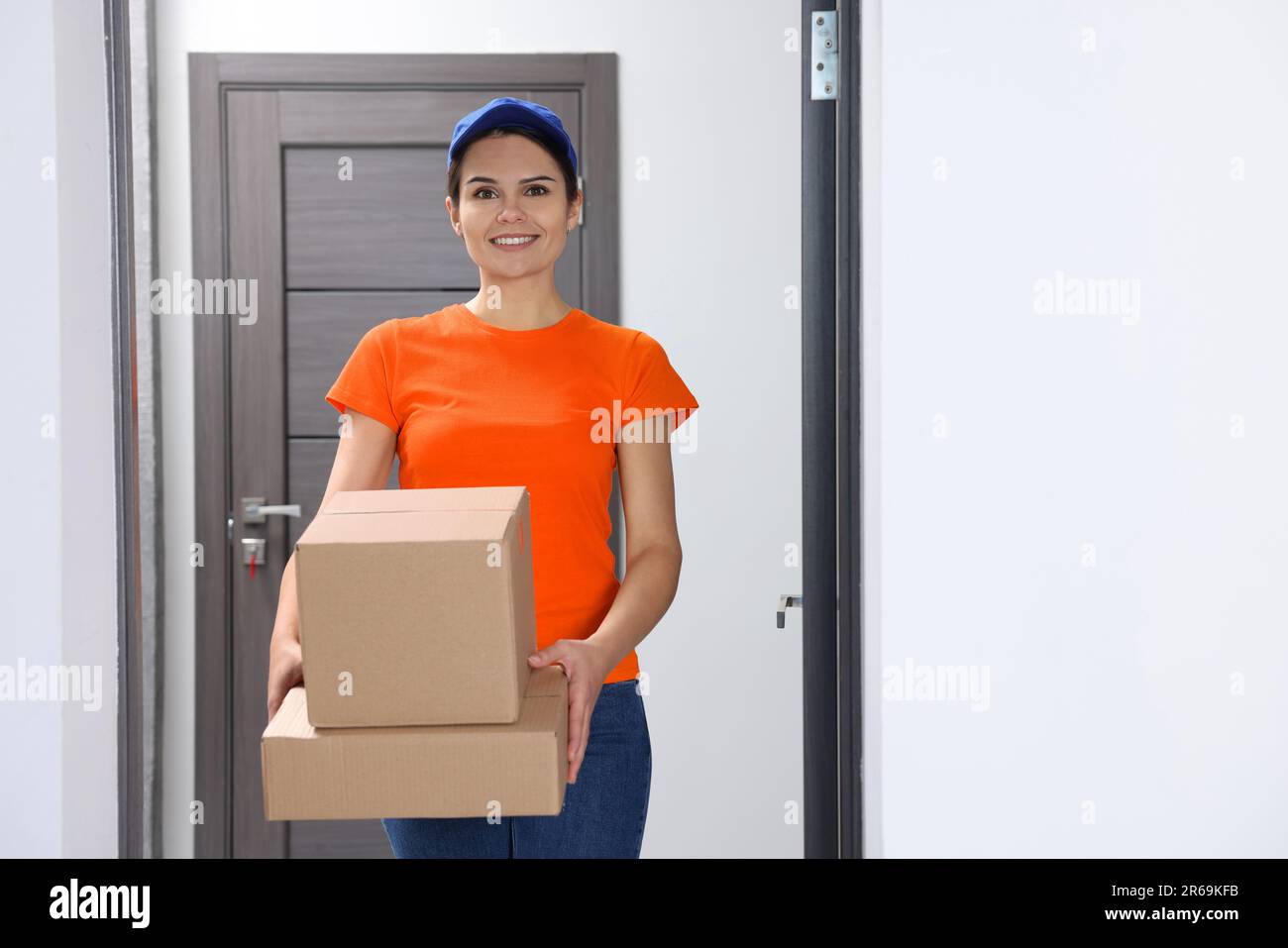 Smiling courier with cardboard boxes in hallway, space for text Stock ...