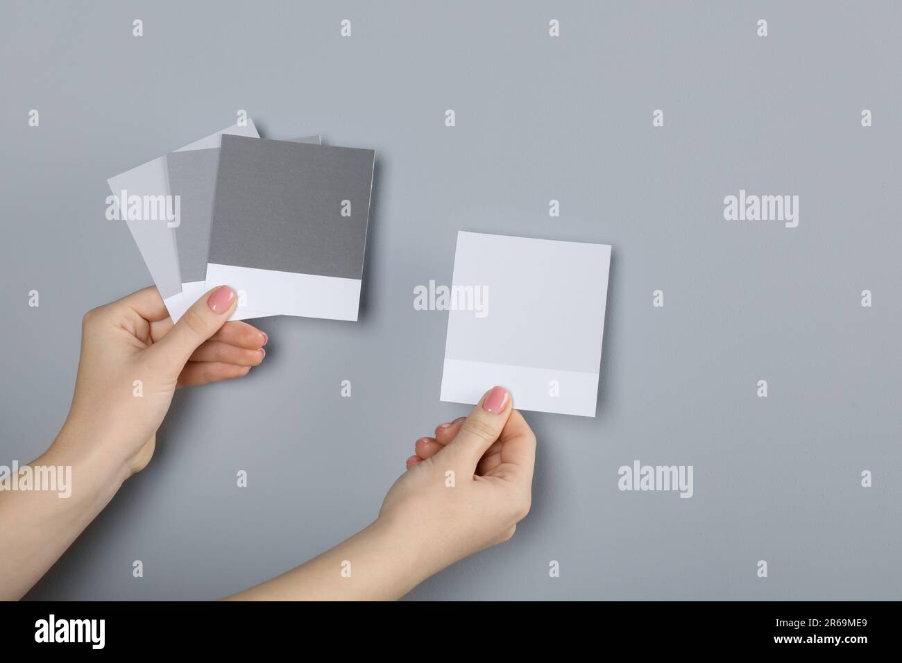 Woman with color sample cards choosing paint shade near grey wall ...