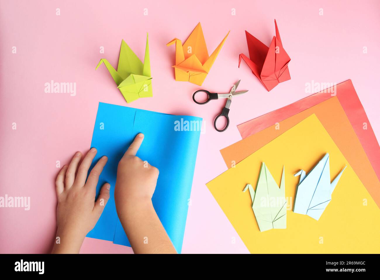 Origami art. Child folding paper on pink background, closeup and top ...