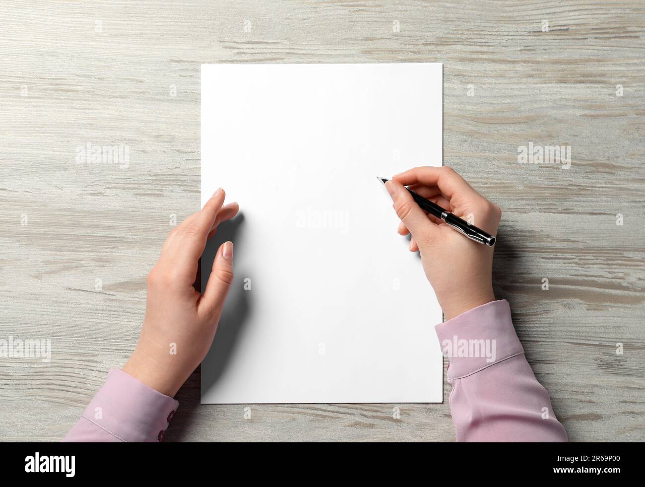 Woman writing on sheet of paper with pen at wooden table, top view ...