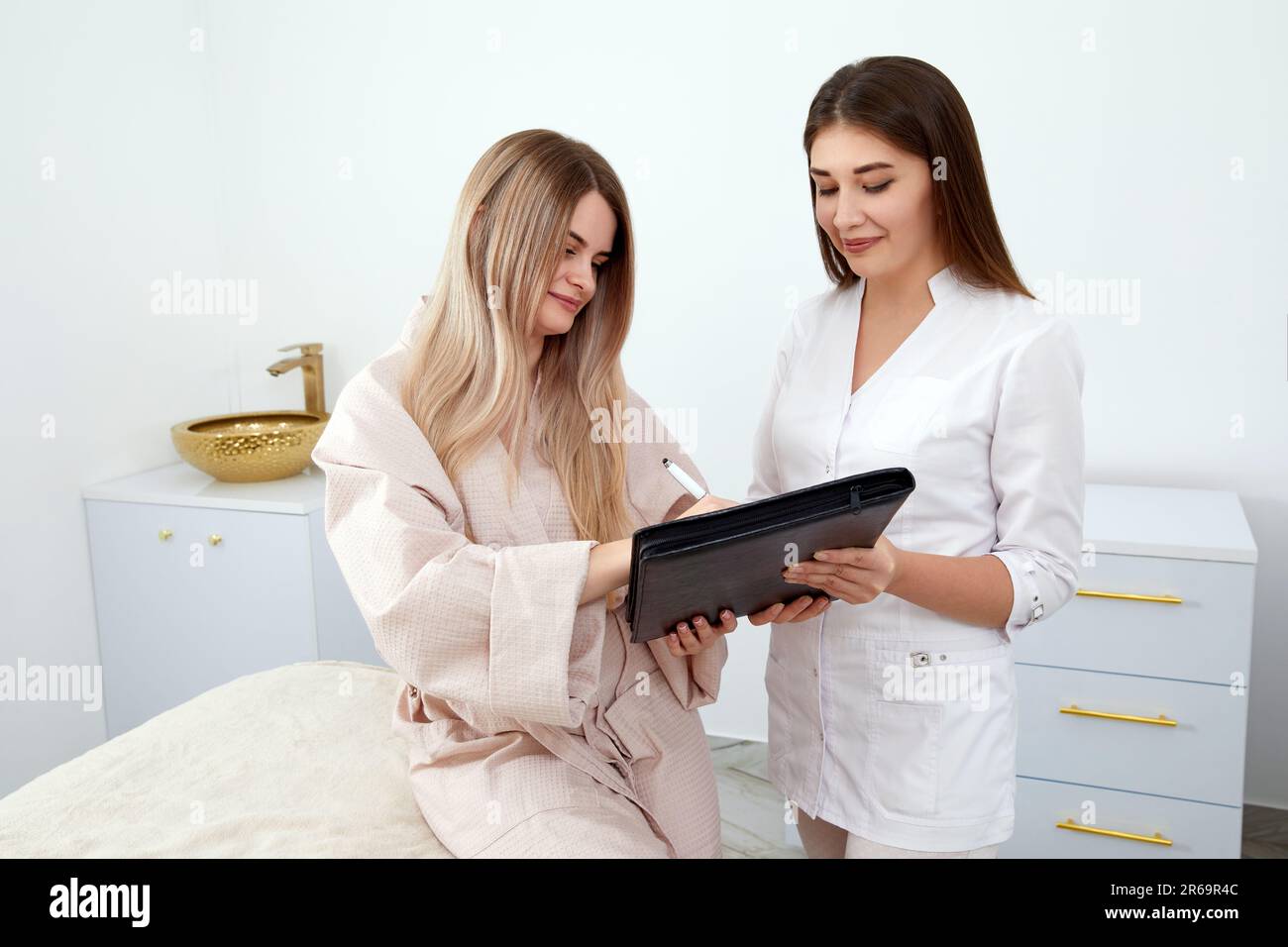 Professional cosmetician and client signing papers before procedure in ...