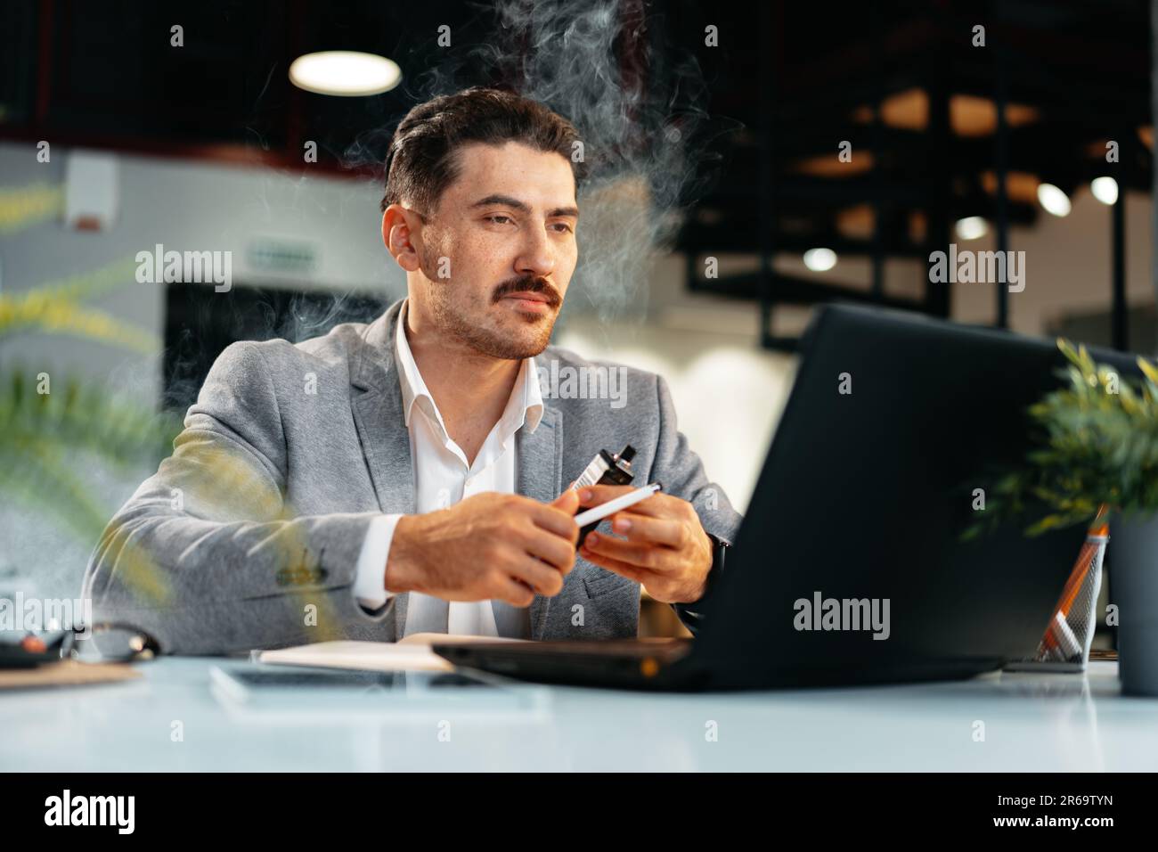 Young businessman smoking an electronic cigarette in his office while ...