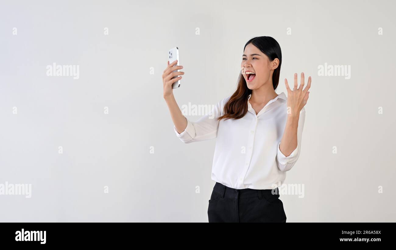 A shocked and excited Asian woman in a white shirt is looking at her ...