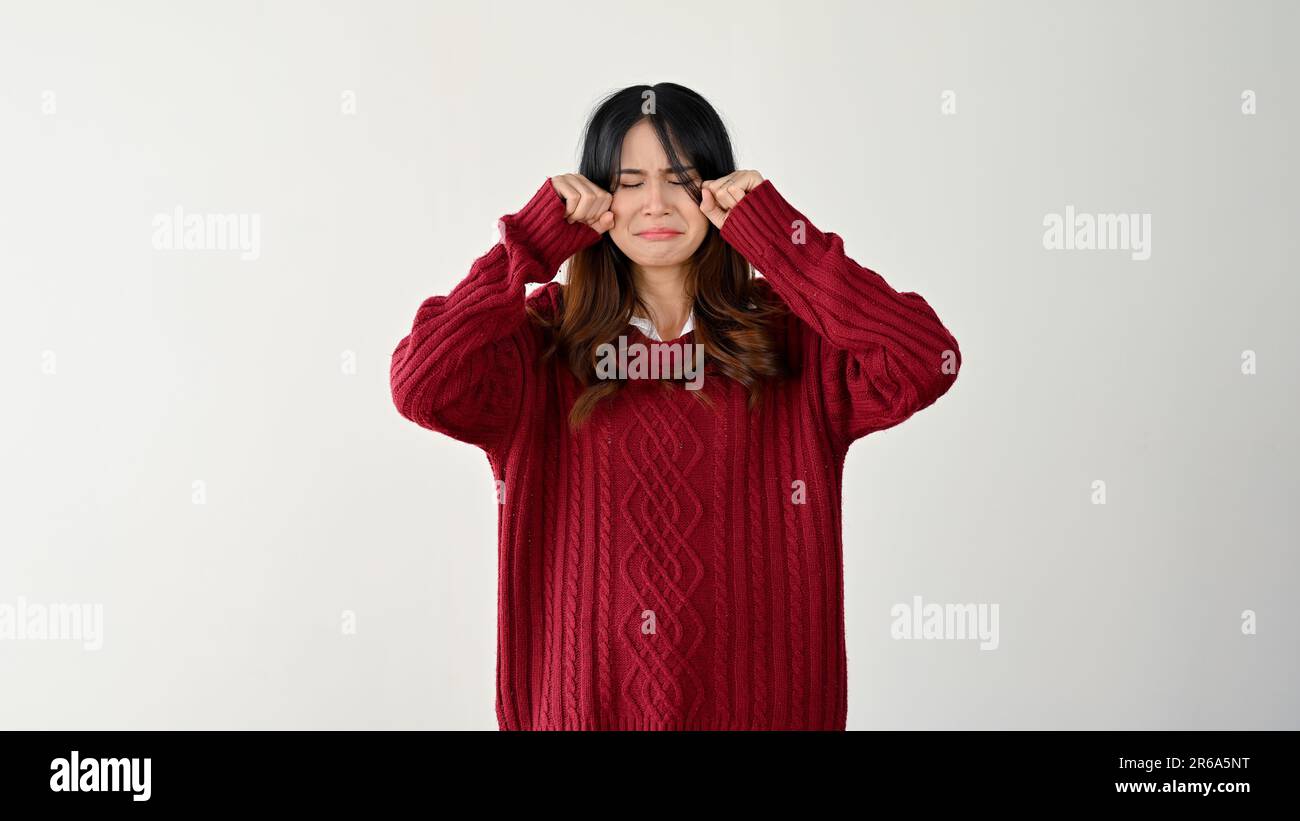 A sad and crying young Asian woman in a red sweater wipes her tears and ...