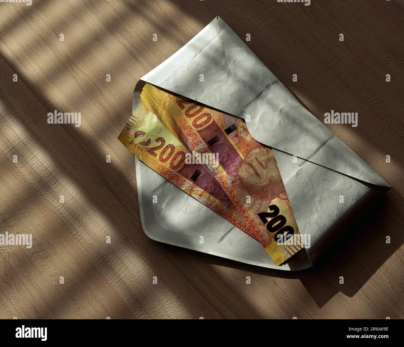 A spreading pile of rand banknotes in an envelope on a wooden surface ...