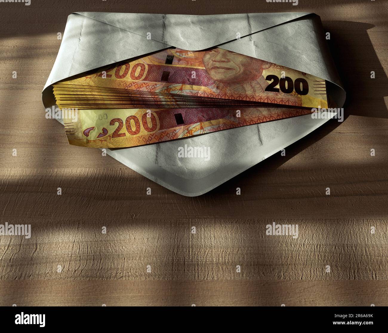 A spreading pile of rand banknotes in an envelope on a wooden surface ...