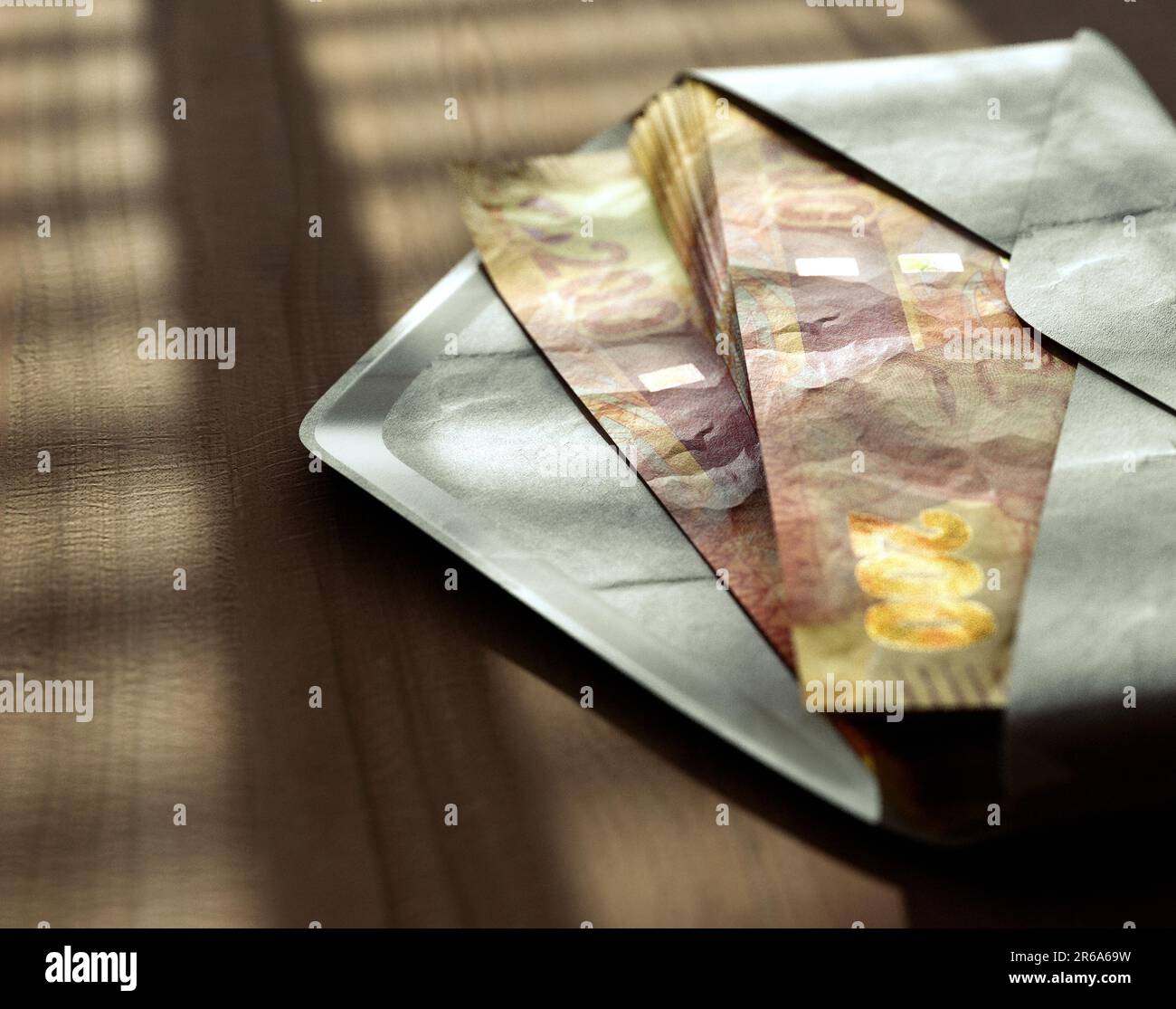 A spreading pile of rand banknotes in an envelope on a wooden surface ...